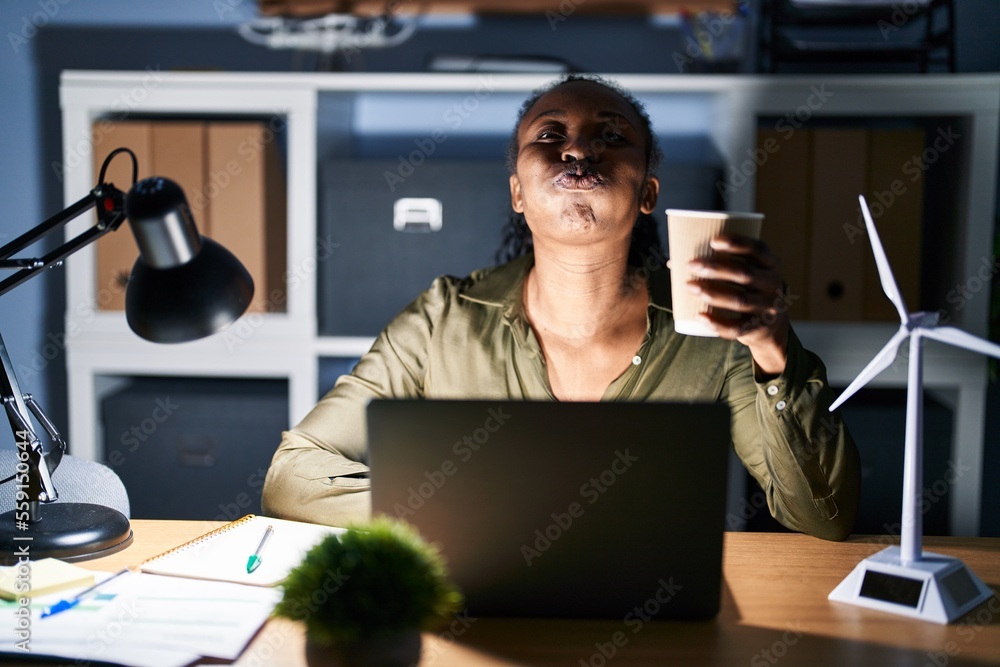 African woman working using computer laptop at night puffing cheeks ...