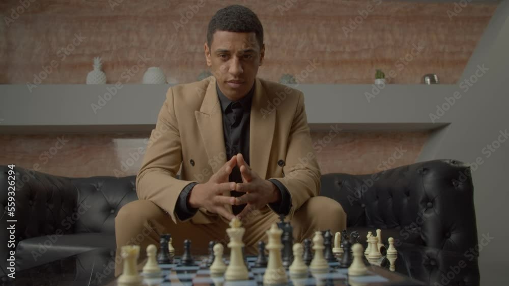 Successful handsome African American male executive moving chess piece on chess board and ...