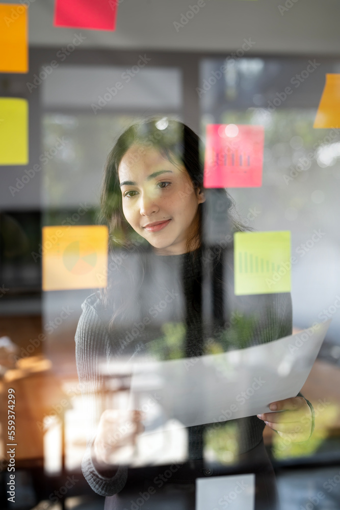 Young smiley attractive businesswoman using sticky notes in glass wall ...