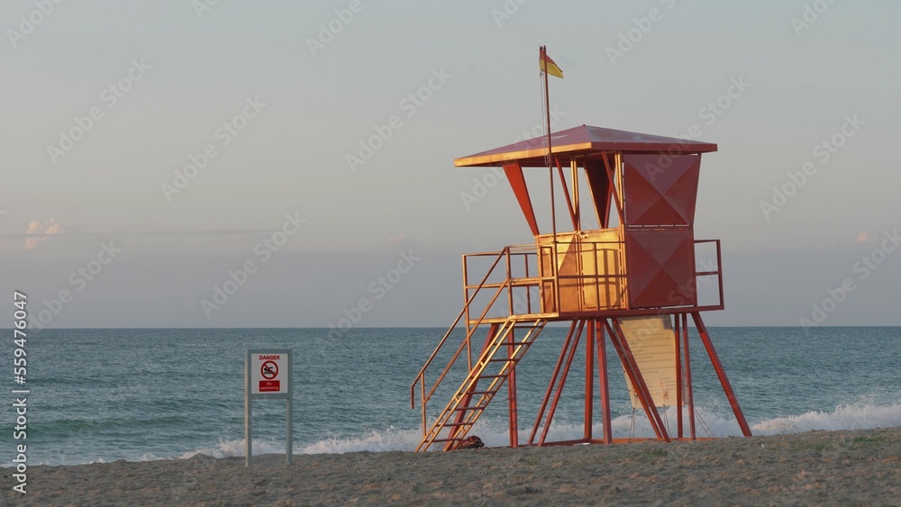 Red lifeguard tower and danger no swim warning placard on empty beach ...