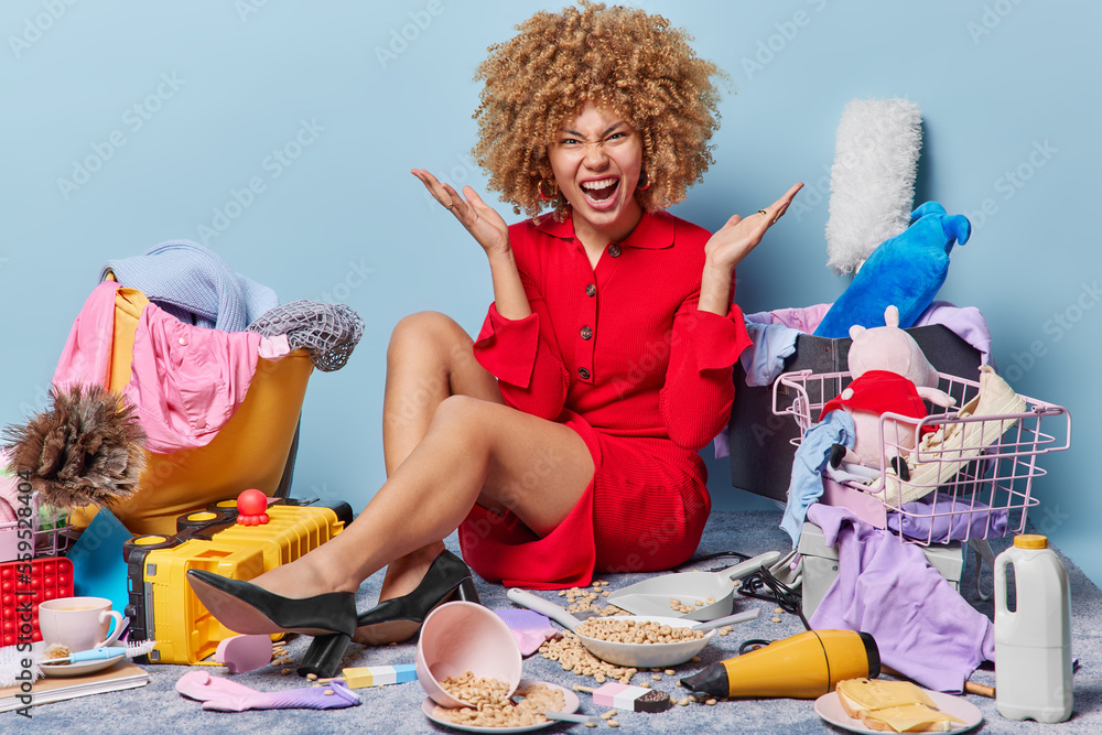Irritated curly lady keeps palms raised and exclaims angrily wears red ...
