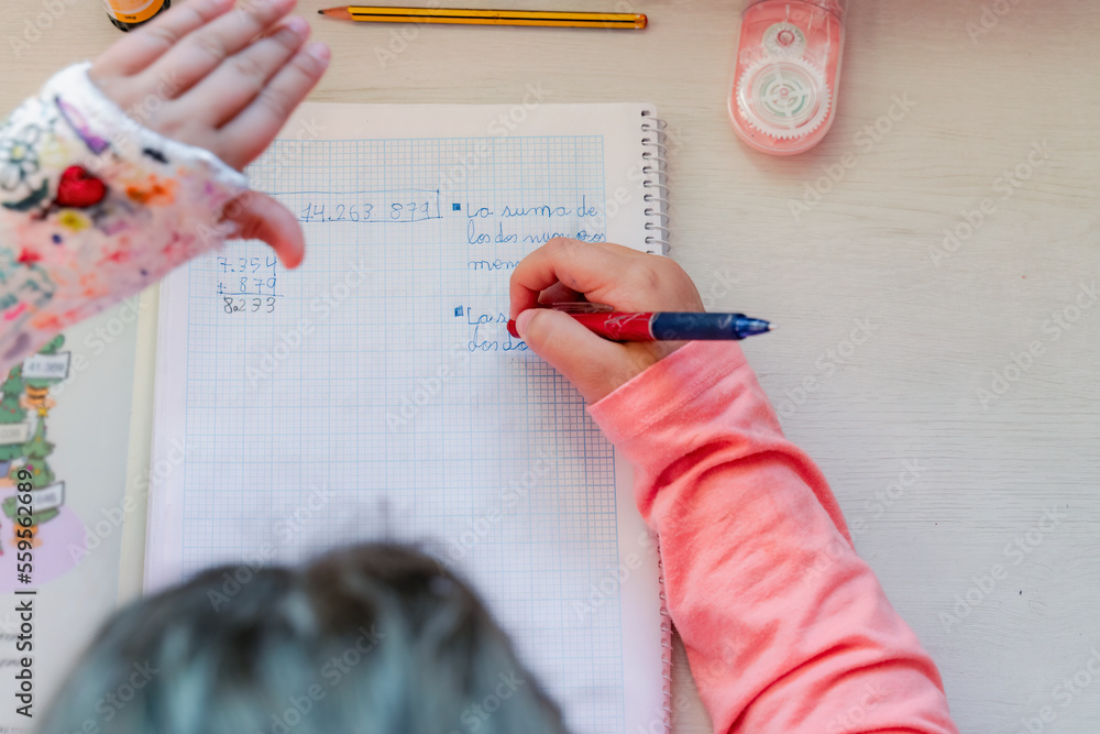 top view of an unrecognisable girl doing maths homework in a notebook ...