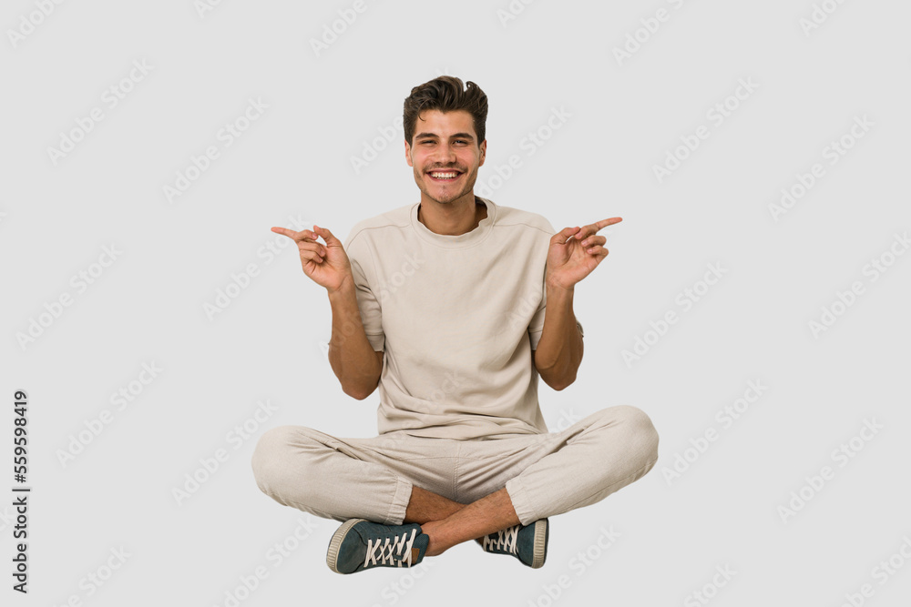 Young caucasian man sitting on the floor isolated on white background ...