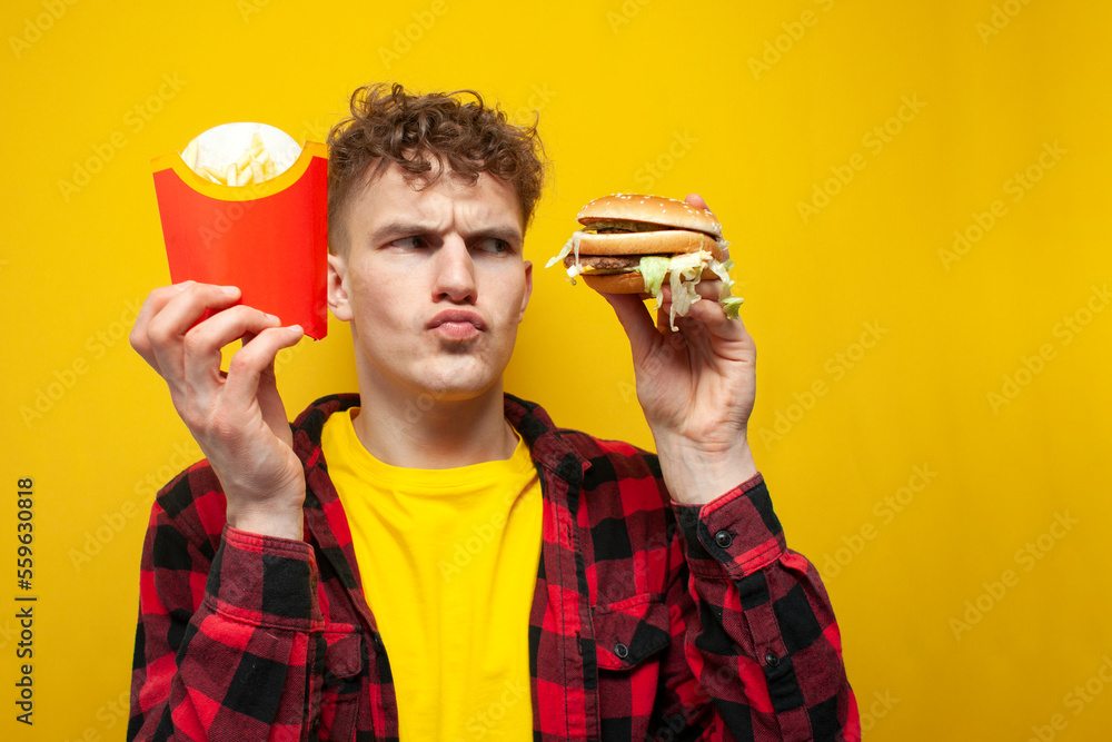 curly guy with fast food holds french fries and looks suspiciously at a ...