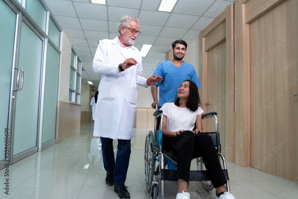 Doctor and male nurse transport a female patient in a wheelchair along ...