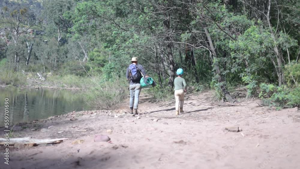 A father and son walk along a river bank in Australia while carrying a ...