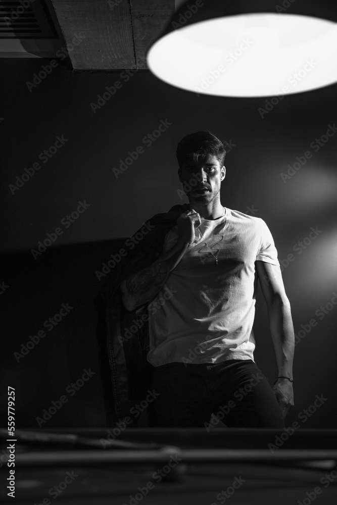 man leaning against wall looking into light, concept photography of handsome man in low light ...