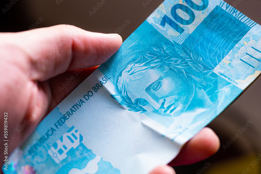 Um homem segurando notas do Real Brasileiro em sua mão. Economia ...