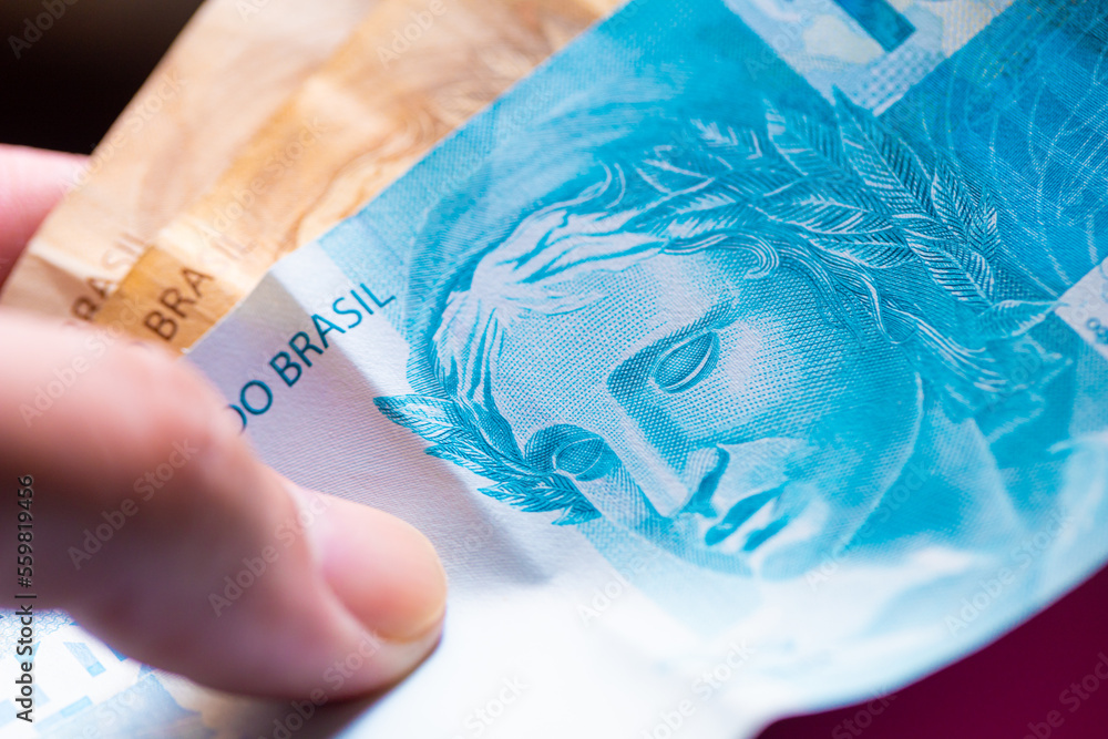 Um homem segurando notas do Real Brasileiro em sua mão. Economia ...