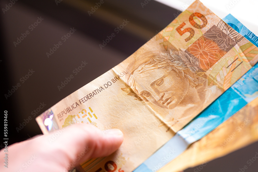 Um homem segurando notas do Real Brasileiro em sua mão. Economia ...