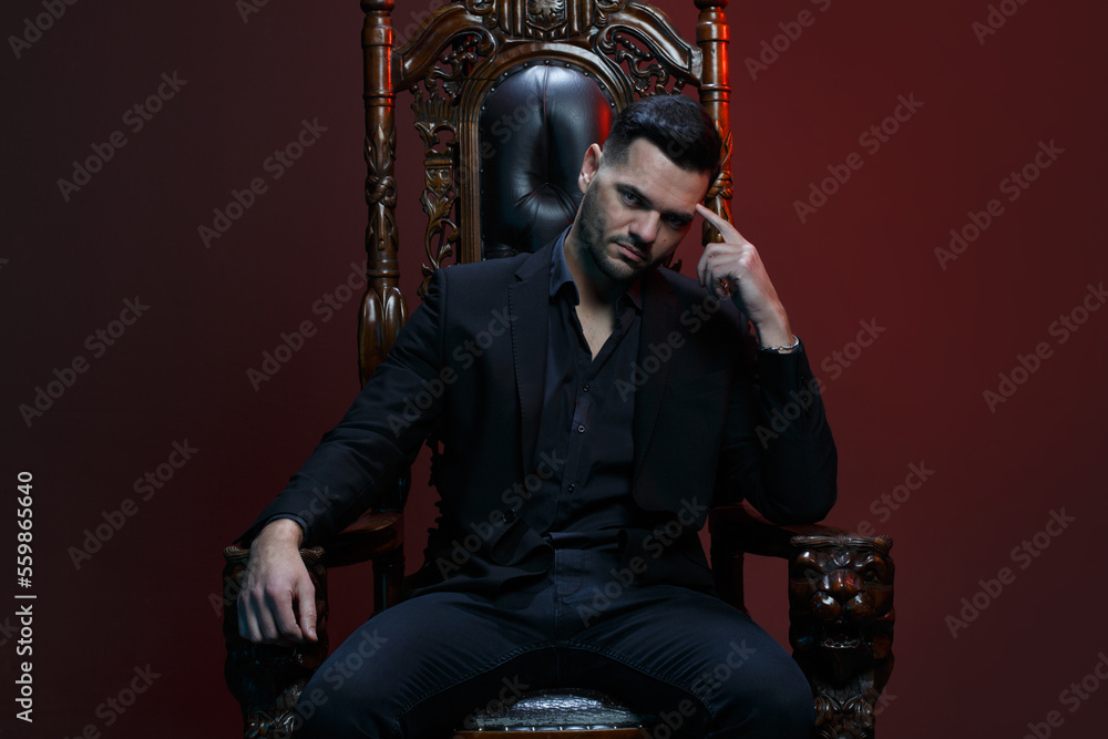 Elegant man in a classic suit sitting in a carved wooden chair against ...