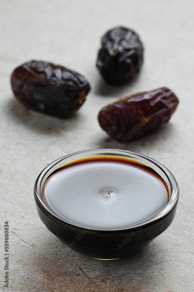 Date syrup in a small glass bowl nearly whole date fruits. Close up ...