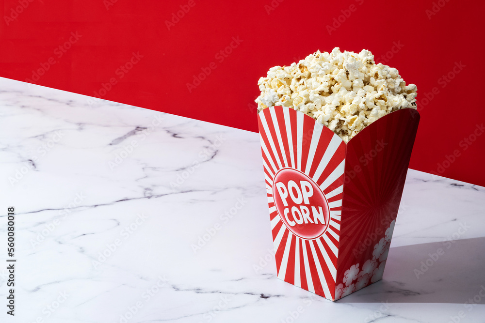 Salted popcorn in carton package on white marble and red background ...