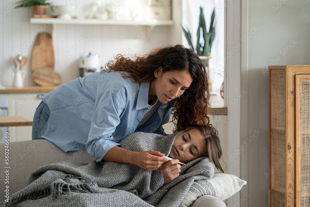 Caring puzzled mother checking sick daughter temperature by handing ...