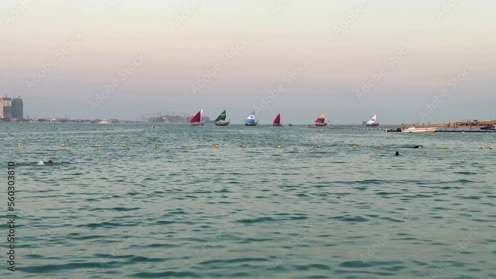 People are swimming in the sea and old lenj traditional Qatar boat are ...