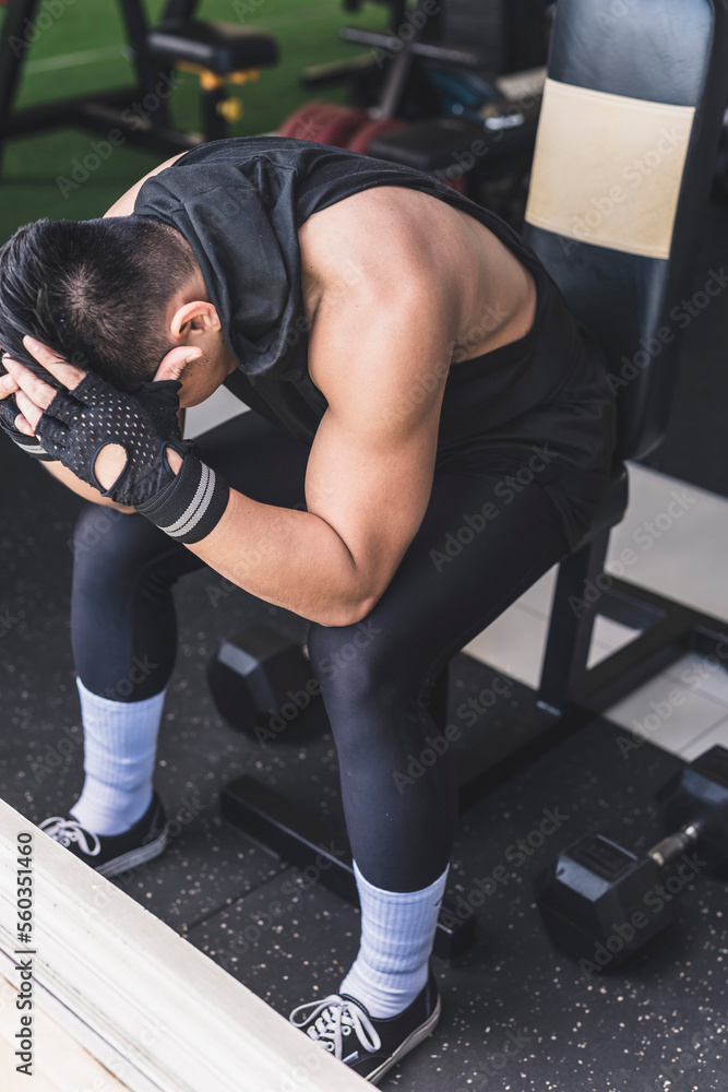 A tanned man sitting on an incline bench, leaning down and covering his ...