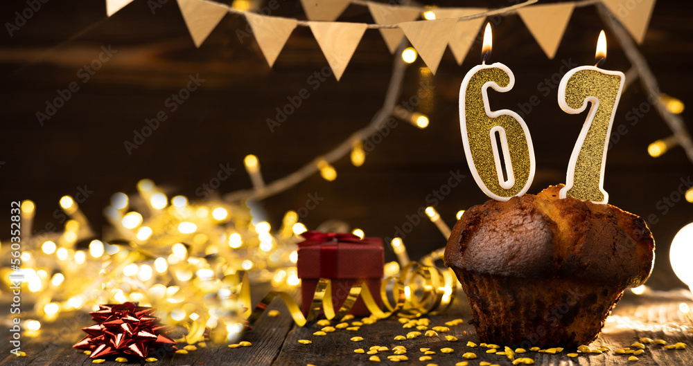 Number 67 golden festive burning candles in a cake, wooden holiday ...
