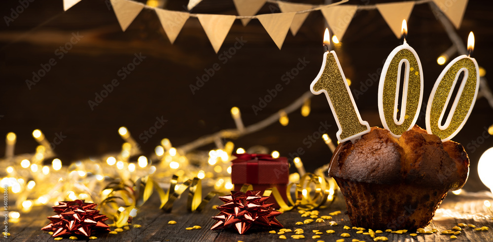 Number 100 golden festive burning candles in a cake, wooden holiday ...