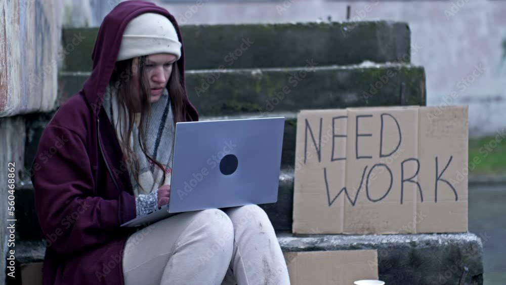 Homeless woman shivering in the cold with a laptop on her lap sits on ...