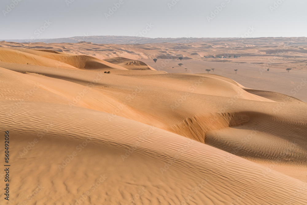 Sand dunes with footprints in them under the blue sky with soft haze on ...