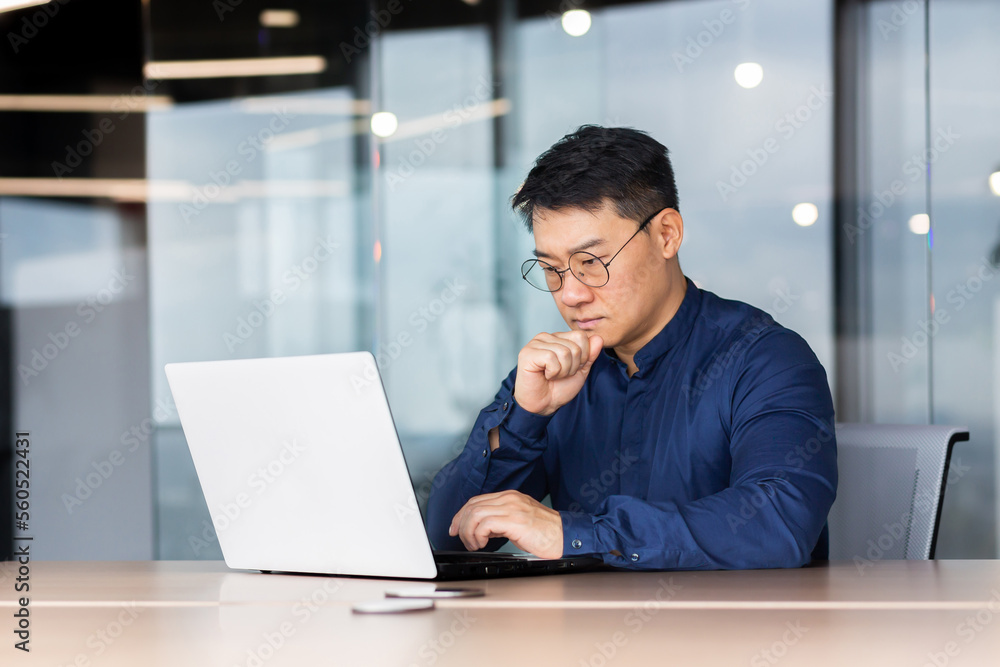 Young concentrated male Asian student studying at laptop. Sitting at ...