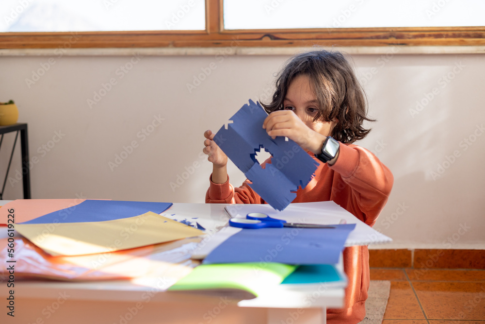 The child makes a snowflake out of colored paper. the boy cuts a ...