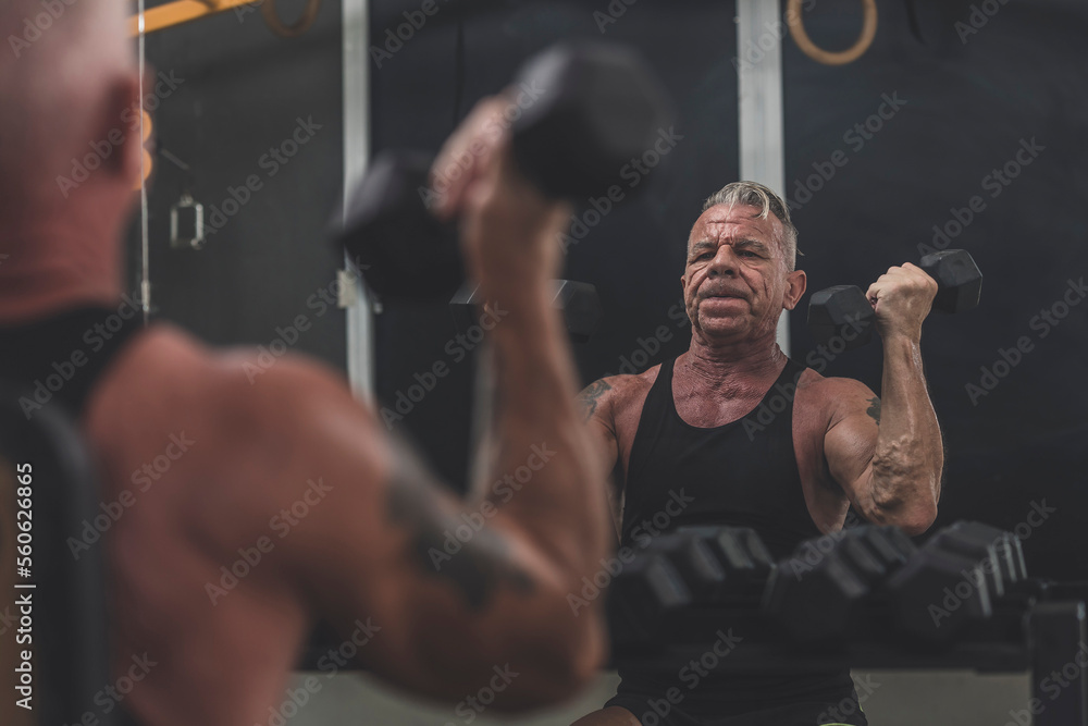 An old German man in his 60s doing seated arnold dumbbell presses at ...
