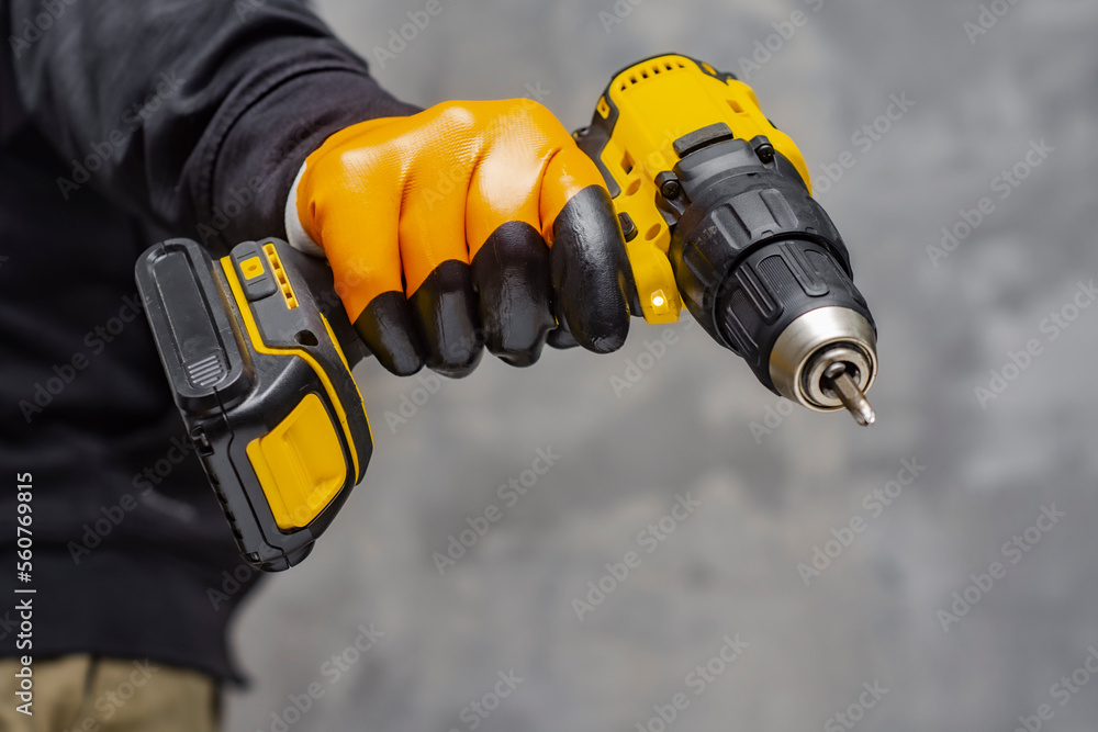 Male worker holds a close-up electric cordless screwdriver in his hands ...