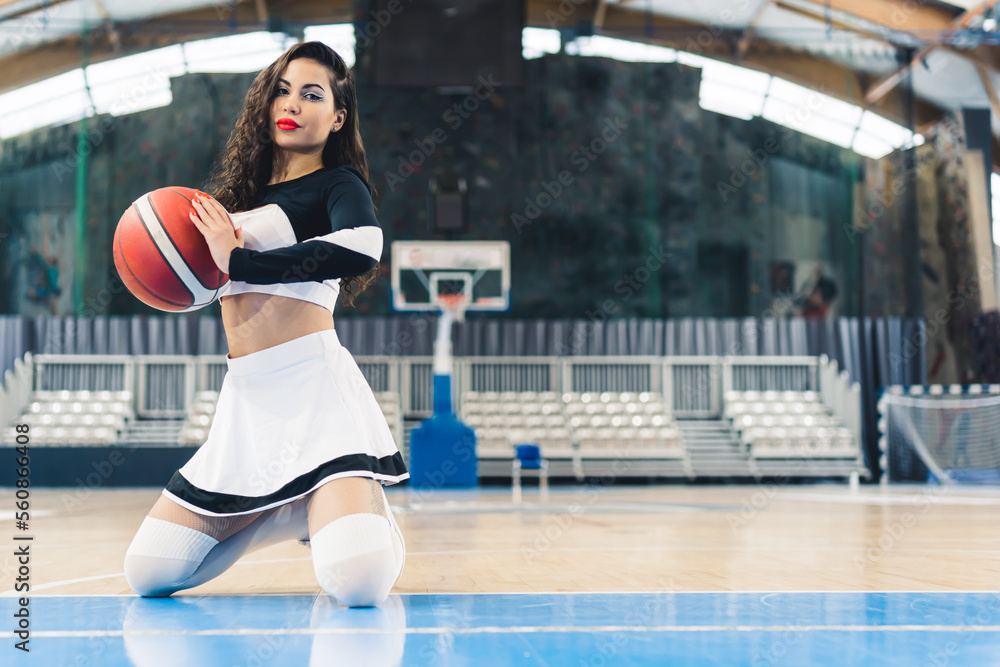 A young, athletic cheerleader sitting on her knees on a basketball ...