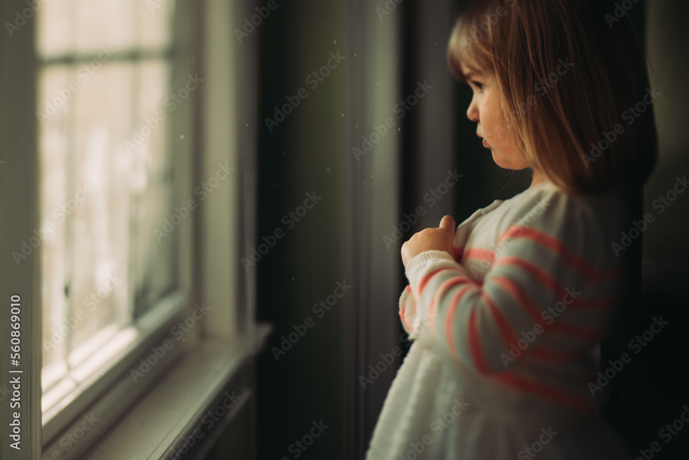 Girl looking out window buttoning sweater Stock Photo | Adobe Stock
