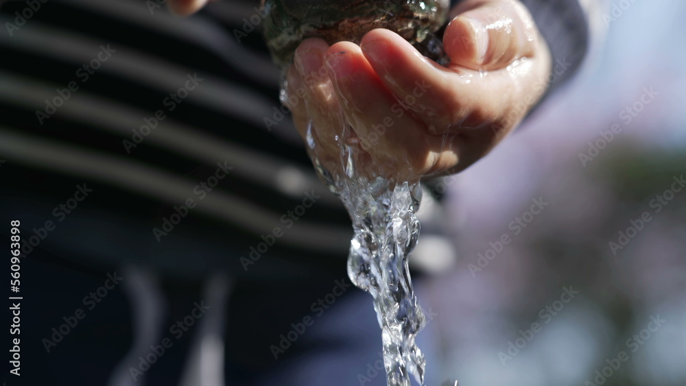 Closeup of flowing water faucet child hand and mouth drinking outdoors at public park. One ...