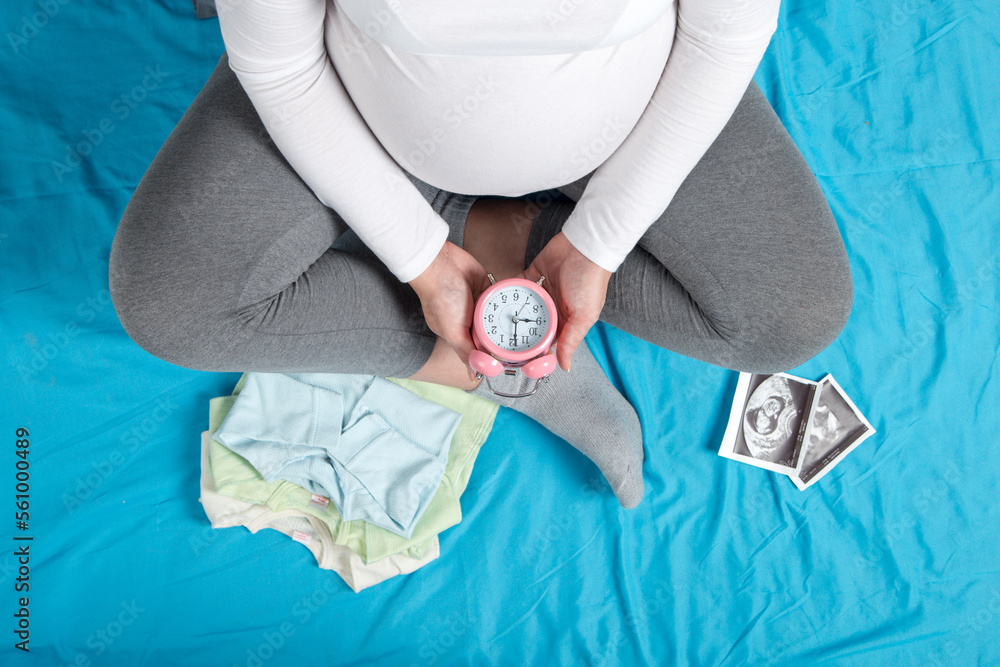 Pregnant girl, children's clothes, ultrasound shots, clock in hand. The ...