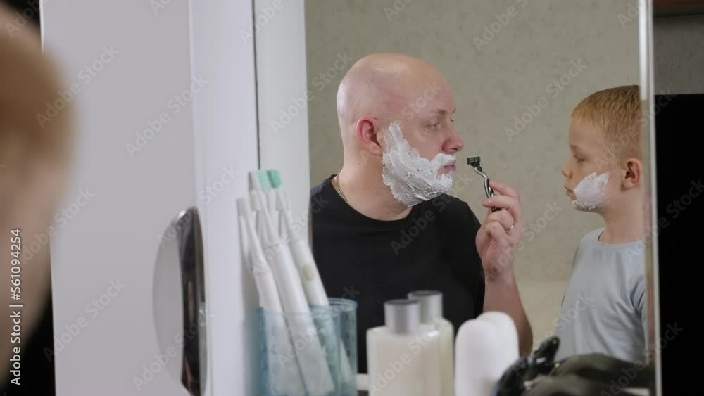 A little boy learns to shave with his dad in the bathroom, he holds a ...