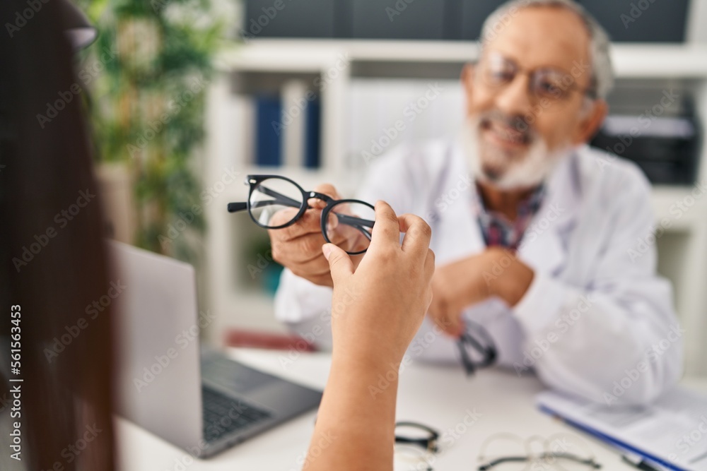 Senior grey-haired man optician holding glasses showing to patient at ...