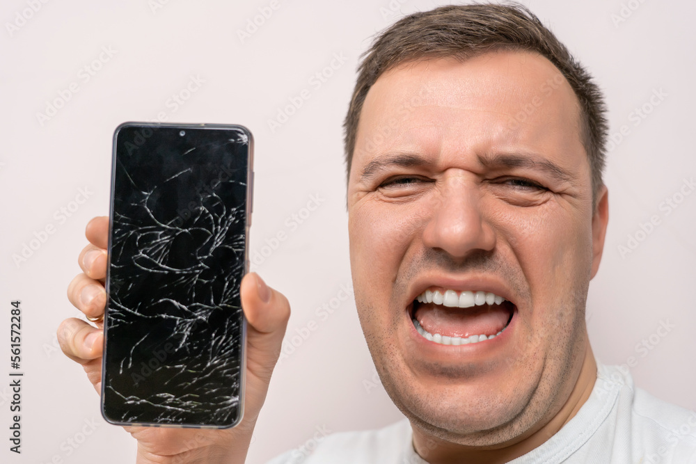 Frustrated man screaming from despair shows smartphone with cracked ...