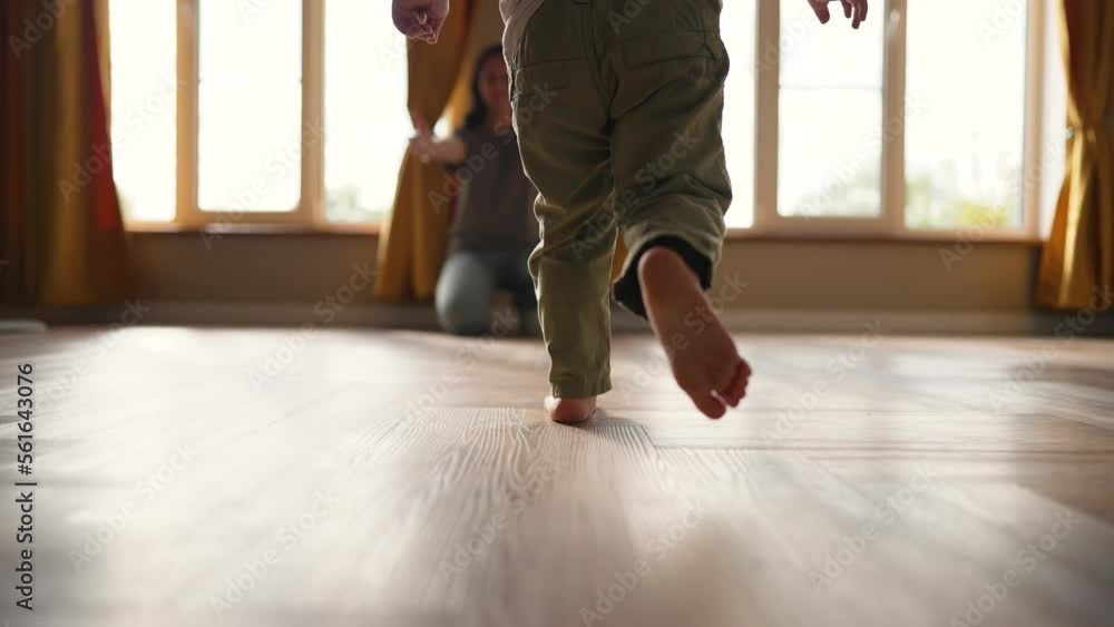 Baby takes first step on floor to his mother with bare feet.Son and ...