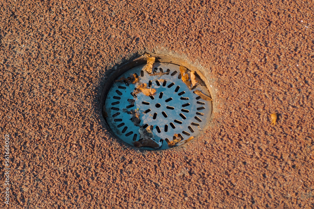 Rounded street sewer drains on the ground in autumn. Iron. Heavy. Rough ...