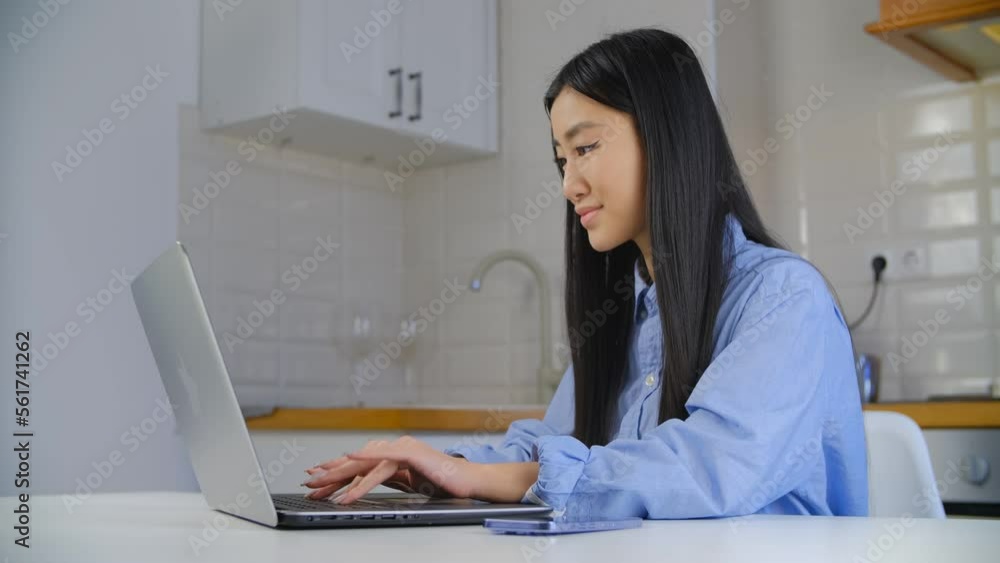 Asian BIPOC female typing text on laptop keyboard in home kitchen ...