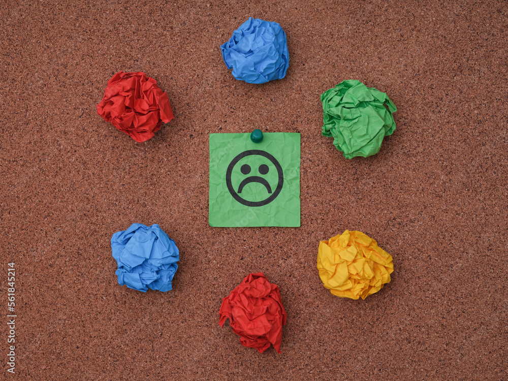 A green paper note with a sad face on it surrounded by colourful ...