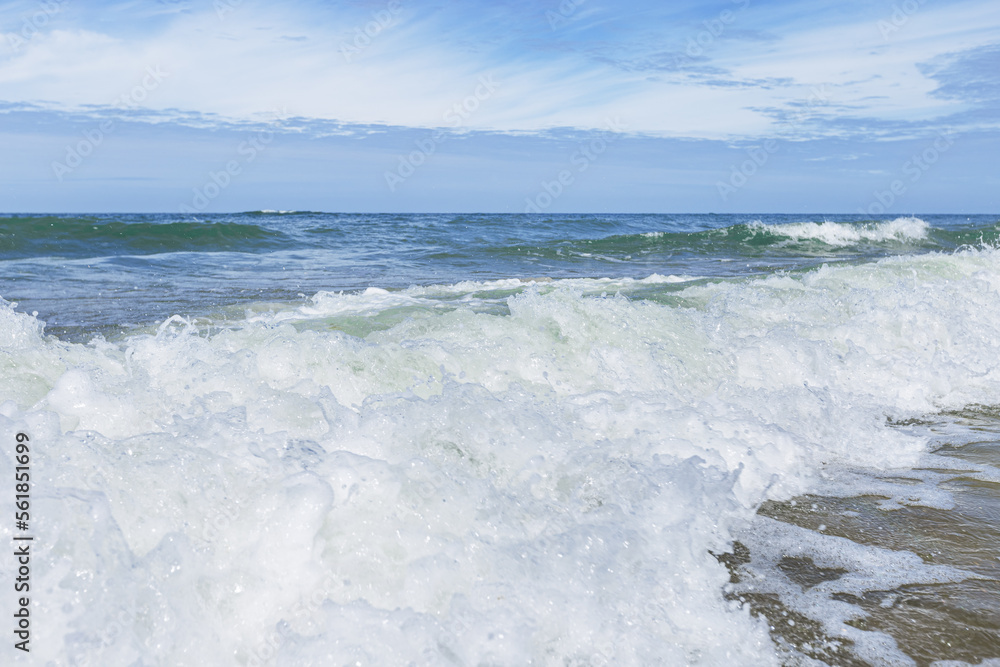 Blue cloudy sky above blue sea water, waves crashing sandy beach, windy ...