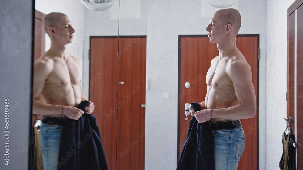 Muscular bald man with shirtless torso looking at his reflection in a ...