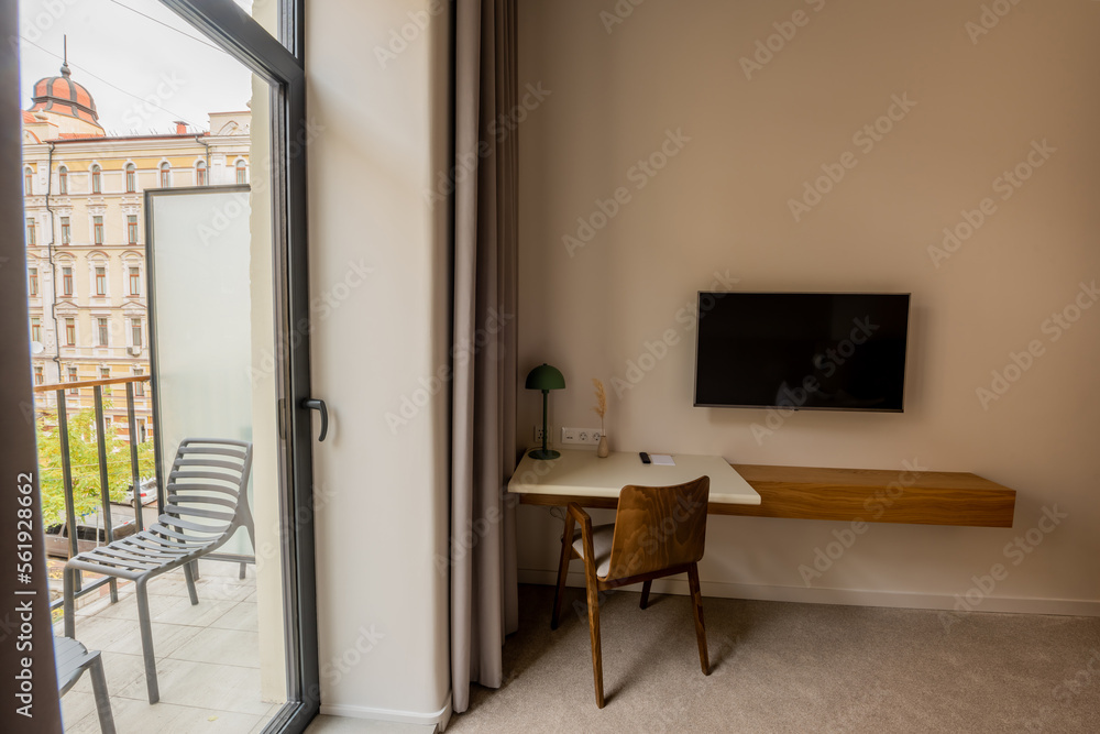 flat tv screen on wall near workspace with chair and balcony in hotel ...