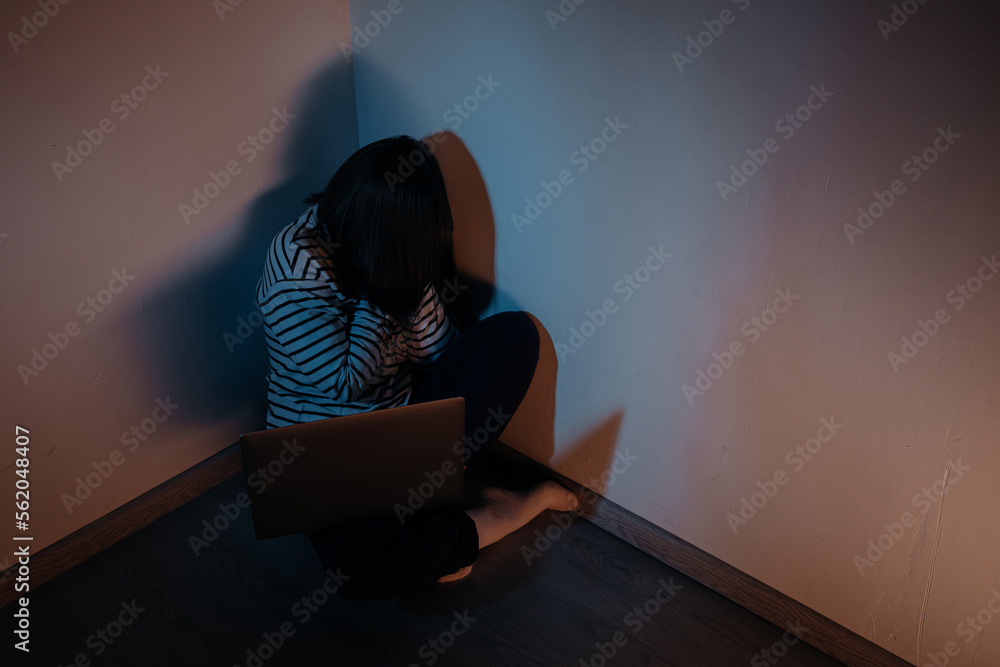 Young teenager female girl sitting with a laptop and crying in a dark ...