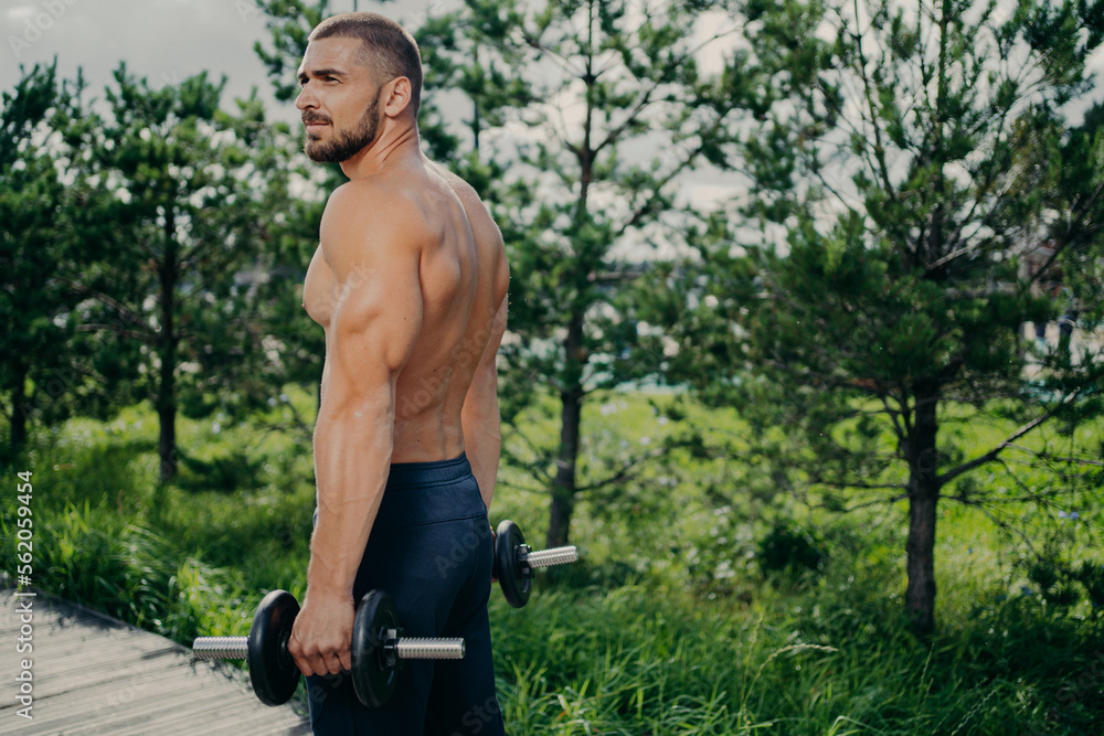 Outdoor shot of muscular strong man prepares for barbell workout, lifts ...