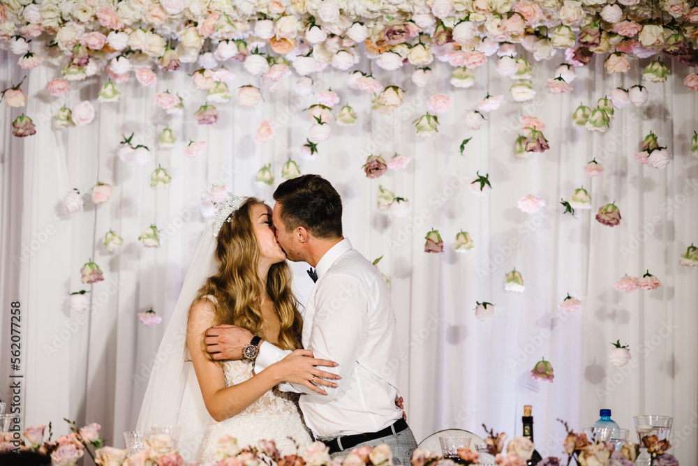 Bride and groom kissing at the table in the banquet hall of the ...