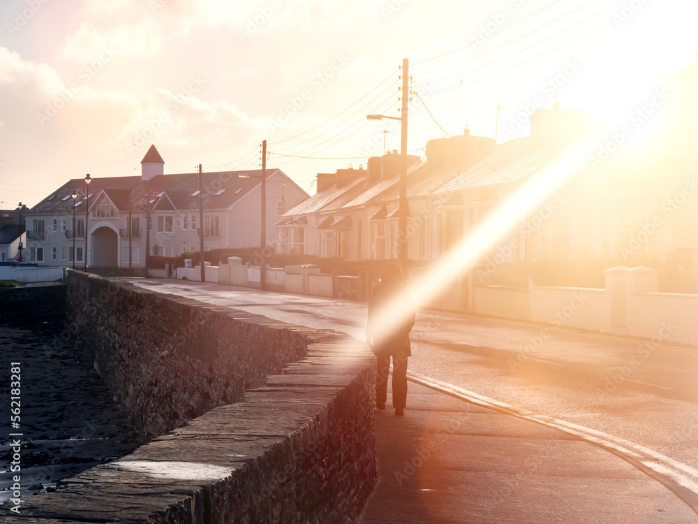 Person walking on a foot path in a street at sunrise. Warm color and ...