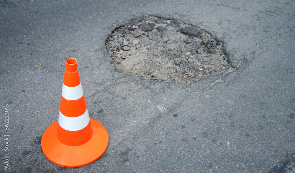 Holes in the road.Asphalt repair. An orange cone indicates damage to ...