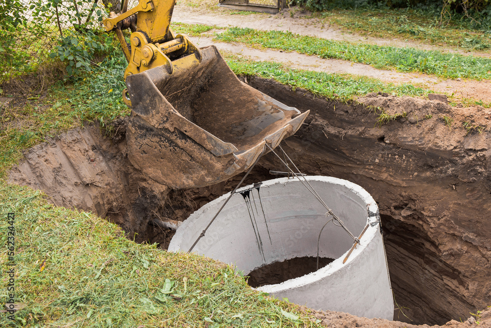 Excavator with a bucket, lowering into the pit on steel cables concrete ...