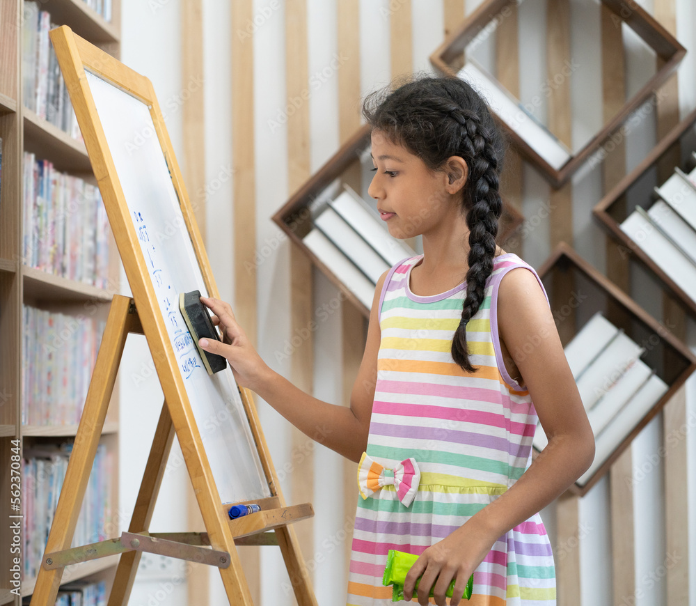 Young girl student standing in classroom erasing text on a whiteboard ...