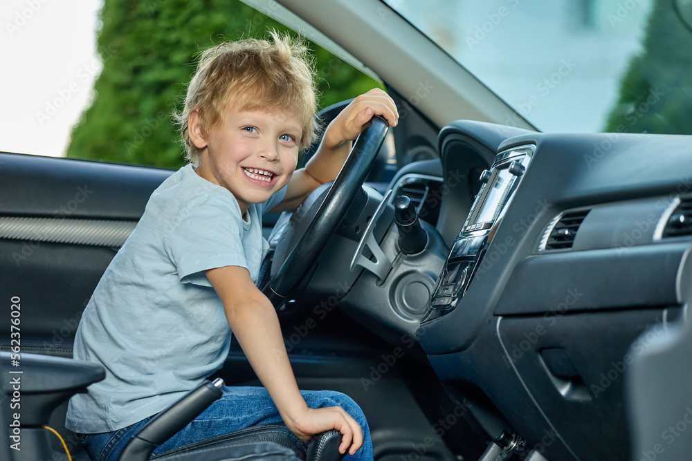 Smiling boy sets in the driver's seat of a car with a black interior ...